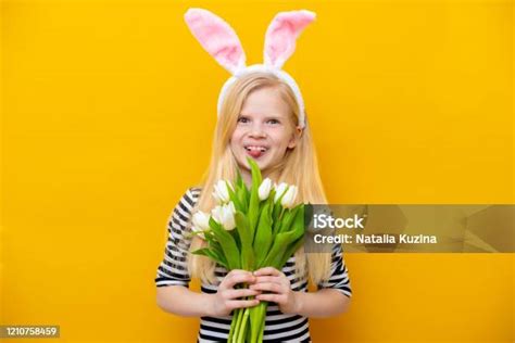 노란색 스튜디오 배경에 머리에 토끼 토끼 귀에 흥분 소녀 쾌활한 미친 미소 행복한 아이는 튤립 꽃다발과 혀를 보여줍니다 부활절과 봄 4월에 대한 스톡 사진 및 기타 이미지