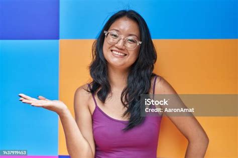 행복한 미소와 승자 표현으로 성취를 축하하는 화려한 배경 위에 서 있는 아시아 젊은 여성 갈색 머리에 대한 스톡 사진 및 기타 이미지 갈색 머리 긍정적인 감정 표현