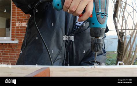 Worker In Warm Work Clothes With Electric Screwdriver Screws Screws