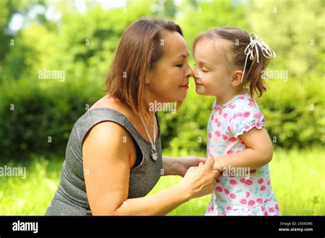 Little Happy Girl And Her Mother Touch Noses Of Each Other In Park