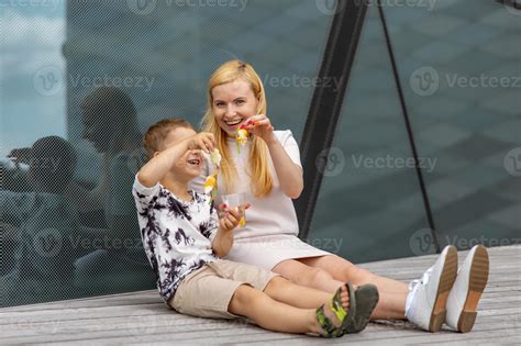 mujer rubia feliz y niño sentado en la terraza y comiendo dulces madre