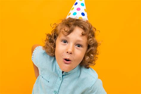 축제 모자를 쓴 유럽의 빨간 머리 곱슬 거리는 소년이 노란색 배경에 카메라를 찡그리고 T 셔츠에 대한 스톡 사진 및 기타 이미지