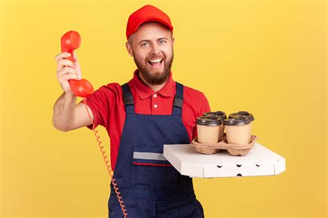 작업복 티셔츠 및 모자를 쓴 남자는 피자와 함께 유선 전화와 커피를 들고 패스트 푸드를 주문하기 위해 전화합니다 남자에 대한 스톡 사진 및 기타 이미지 Istock