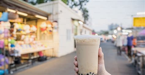 한 젊은 여성이 대만의 야시장에서 갈색 설탕 거품 밀크티의 플라스틱 컵을 들고 있습니다 사진 Unsplash의 아이스 티 이미지