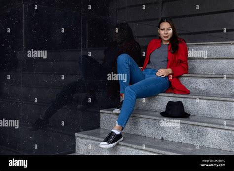 Portrait Of Young Latin American Woman Sitting On Stairs Poses With