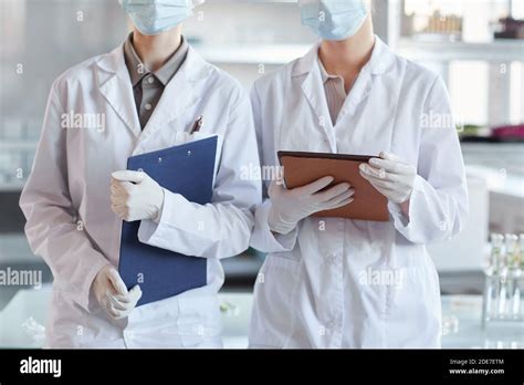 Cropped Portrait Of Two Female Scientists Wearing Face Mask And Holding Clipboards While