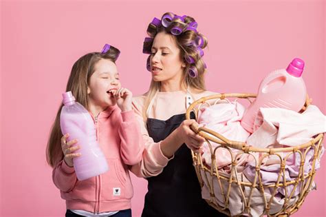 미소 짓는 어린 소녀는 세탁물을 들고 풀고있는 집안일로 어머니를 돕습니다 여자는 손에 옷의 고리 버들 바구니를 들고있는 동안