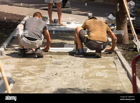 Young Working Men Make A Path Laying Paving Slabs On A Sand Base On A