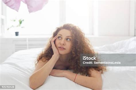 곱슬 머리와 꿈꾸는 듯한 여자의 실내 샷 침대에 잠겨있는 식 침실에서 자유 시간을 보낸다 하루에 대 한 그녀의 계획에 대 한 고민 수 면 전에 뭔가 대해 생각 하는 아름