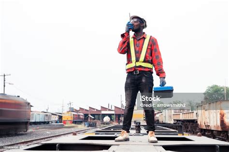 헬멧 숲 및 안전 조끼를 입은 아프리카 기계 엔지니어 기술자가 렌치를 사용하여 라디오 통신 이나 무전기로 말하는 기차를 수리하고 있습니다 개념에 대한 스톡 사진 및 기타
