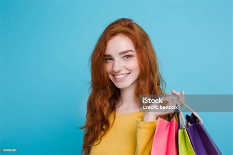 쇼핑 개념세로 젊은 아름 다운 매력적인 Redhair 여자 쇼핑 가방 카메라를 보고 미소를 닫습니다 블루 파스텔 배경입니다 공간