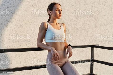 어두운 머리와 포니 테일 흰색 상의와 베이지 색 레긴을 입고 젊은 성인 자신감 여성은 멀리 찾고 훈련 후 휴식을 취하고 야외에서