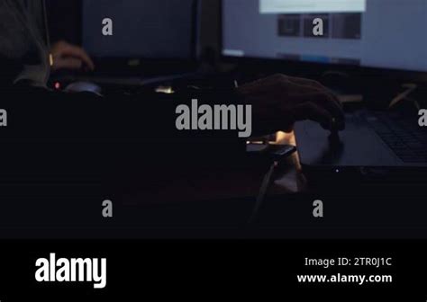male hand of hacker in hood cracking code using computers in dark room