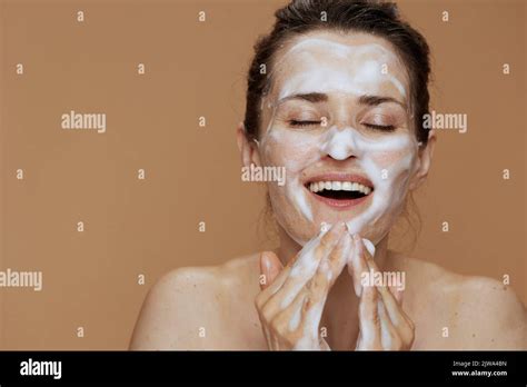 Happy Young Woman With Foaming Face Wash Washing Face Against Beige