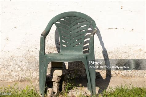 플라스틱 오래된 깨진 의자는 햇볕에 여름 별장에있는 집의 흰 벽 오래된 의자의 배경에 서 있습니다 0명에 대한 스톡 사진 및