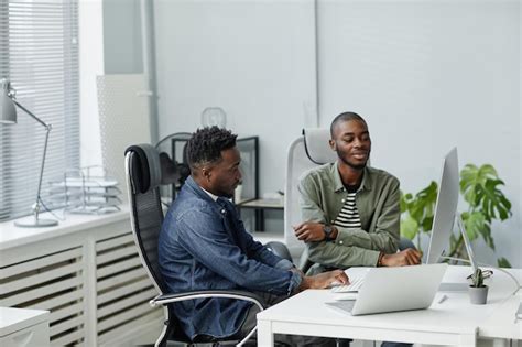 Premium Photo Two Young Confident Programmers Sitting By Desk In Front Of Computer Monitor
