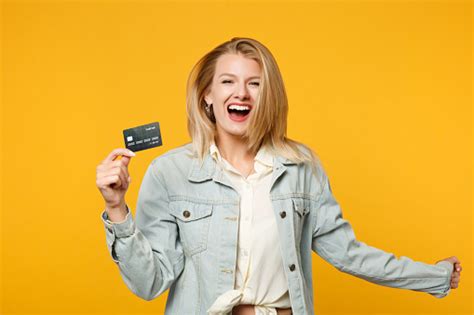 스튜디오에서 노란색 오렌지 배경에 고립 된 신용 카드를 들고 카메라를 찾고 데님 캐주얼 복장에 행복 한 젊은 여자의 초상화