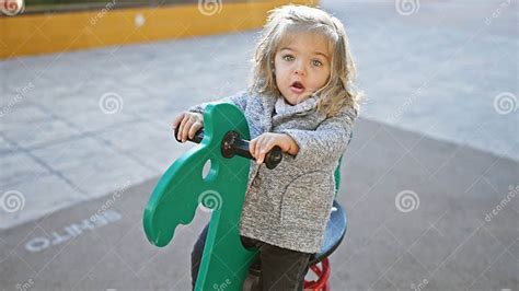 A Curious Blonde Girl In A Park Playing On A Green Spring Rider