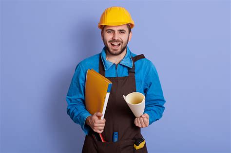 스튜디오에서 파란 배경 위에 고립 된 감정적 인 잘 생긴 빌더의 초상화 종이 케이스를 들고 입을 넓게 열고 외치고 수염을 기고
