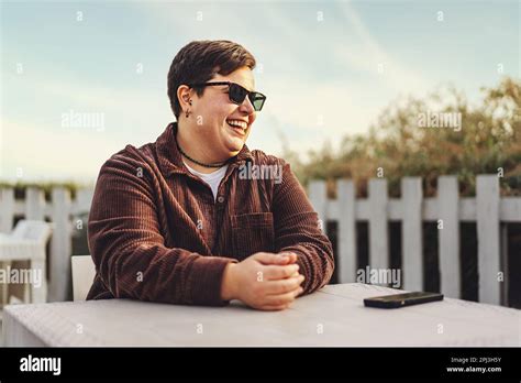 Smiling Plus Size Non Binary Person With Sunglasses At An Outdoor Cafe