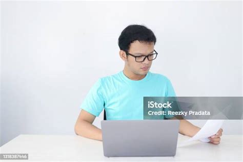 젊은 아시아 남자는 심각 하 고 테이블에 노트북및 문서에 작업 할 때 초점을 맞추고있다 파란색 셔츠를 입은 인도네시아 남자 25