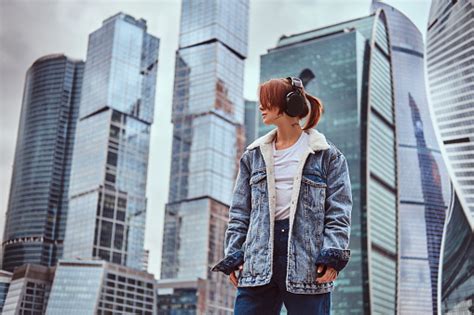 그녀의 얼굴에 문신과 힙 스 터 소녀 옷을 입고 헤드폰은 흐린 아침에 모스크바의 고층 빌딩 앞에서 음악을 듣고 가을에 대한 스톡