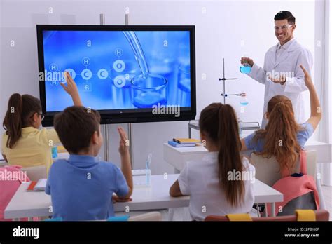 Teacher Holding Flask With Solution Near Interactive Board In Classroom During Practical Lesson Teacher Holding Flask With Solution Near Interactive Board In Classroom During Practical Lesson