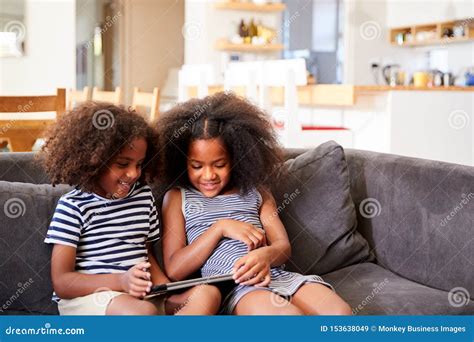 Brother And Sister Sitting On Sofa At Home Playing With Digital Tablet