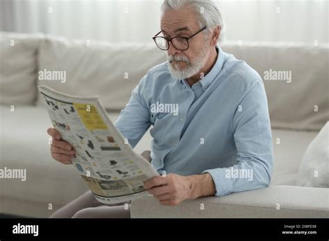 Portrait Of Grandpa With Stylish Glasses Reading Newspaper On Sofa