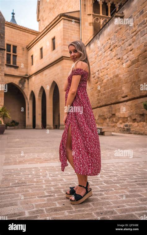 A Blonde Caucasian Girl Wearing A Red Dress In Front Of A Medieval