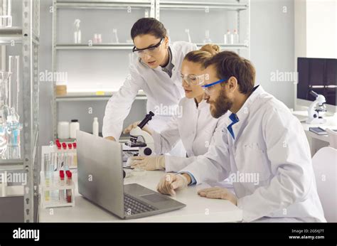 Group Of Young Scientist Testing Sample With Microscope Discussing