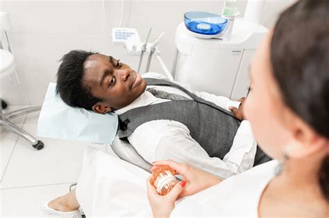 치과 진료소에서 근관을 치료하는 젊은 여성 치과 의사 입을 벌리고 치과 의자에 누워 나쁜 치아를 가진 젊은 아프리카 계 미국인 남성 개념에 대한 스톡 사진 및 기타 이미지