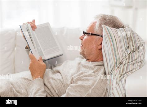 Senior Man Lying On Sofa And Reading Book At Home Stock Photo Alamy