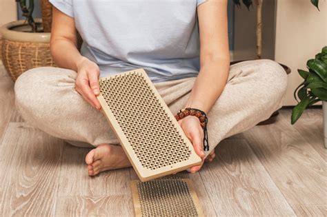 한 여성이 손톱이 달린 나무 사두 보드를 들고 바닥에 앉아 있다 손톱에 서 연습 인도 관행 Mental Wellbeing에 대한