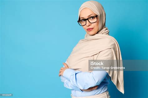 히잡에 덮여 머리와 복사 공간과 파란색 배경에 고립 된 안경을 입고 아름다운 무슬림 여성 가리기에 대한 스톡 사진 및 기타