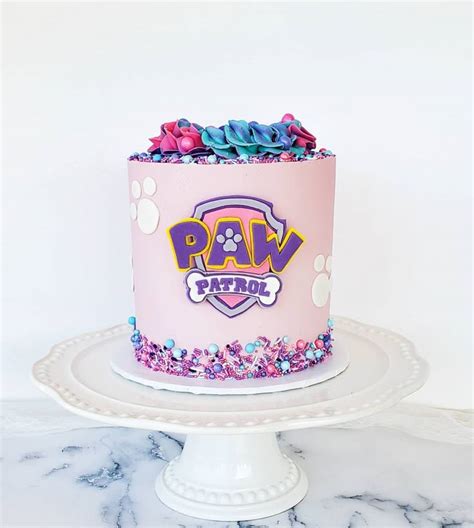 A Pink Paw Patrol Birthday Cake On A White Pedestal With Blue And