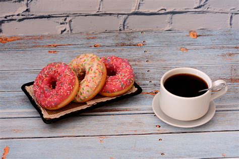 흰색과 분홍색 유약으로 된 도넛 세 개가 블랙 커피 한 잔 옆에있는 나무 테이블에 토핑을합니다 3가지 개체에 대한 스톡 사진 및 기타 이미지 Istock