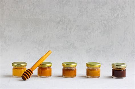 다른 종류와 꿀의 색상과 금속 캡 다섯 작은 유리 항아리 라인과 나무 숟가락 분리 및 복사 공간 회색 시멘트 배경에 넣어 건강
