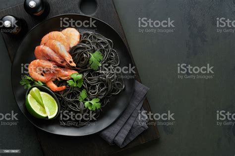 검은 스파게티 파스타 새우는 어두운 콘크리트 테이블 배경에 검은 접시에 있다 새우를 곁들인 오징어 먹물 파스타 파스타 해산물
