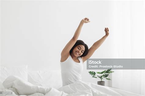 활력과 에너지로 가득찬 행복한 흑인 여성 깨어나고 손을 뻗고 침대에 앉아 미소를 짓고 공간을 복사합니다 스트레칭에 대한 스톡 사진 및 기타 이미지 Istock