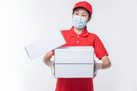 빨간 모자 빈 티셔츠 유니폼 얼굴 마스크 장갑을 낀 의식이 있는 젊은 배달원의 이미지는 밝은 회색 배경 스튜디오에 격리된 빈