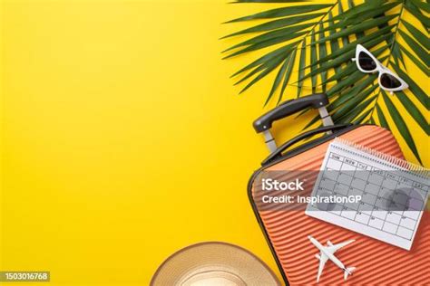 여름 방학 개념입니다 비행기 모델과 달력이 있는 여행 가방의 오버헤드 뷰 사진에는 야자수 잎 선글라스 밀짚모자가 있는 격리된 밝은 노란색 배경에 복사 공간이 있습니다 달력에
