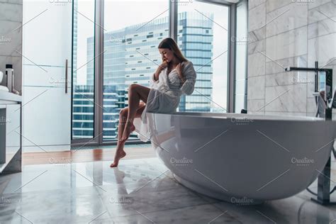 Pretty Slim Woman Wearing Bathrobe Sitting On Edge Of Bathtub Filling