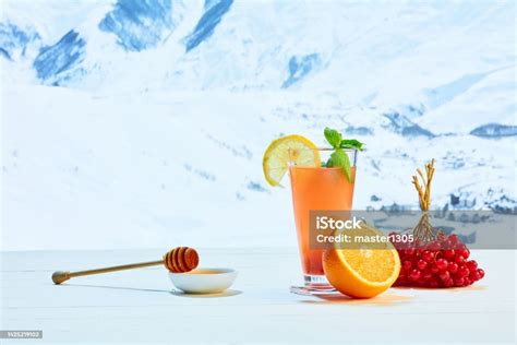 오렌지 차 또는 칵테일 딸기와 꿀을 넣은 유리는 겨울 눈 덮인 산의 풍경을 배경으로 흰색 테이블에 있습니다 건강 보살핌 사랑 0