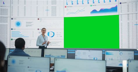 백인 여성 데이터 과학자가 사무실에서 그린 스크린 크로마키로 큰 디지털 스크린에 프레젠테이션을 하고 있다 데스크톱 컴퓨터 뒤에서 듣고 있는 딥 러닝 회사 직원들의 팀 책상에