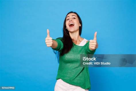 녹색 캐주얼 옷을 입고 카메라를 찾고 스튜디오에서 밝은 파란색 벽 배경에 고립 된 엄지 손가락을 보여주는 쾌활한 웃음 젊은 여성의 초상화 사람 라이프 스타일 개념입니다 복사