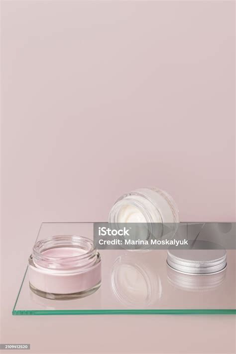 분홍색과 흰색 얼굴과 바디 스킨 케어 크림은 유리 표면에 열린 유리 화장품 항아리에 담겨 있으며 선반에 떠 있습니다 수직 보기 복사 공간입니다 0명에 대한 스톡 사진 및