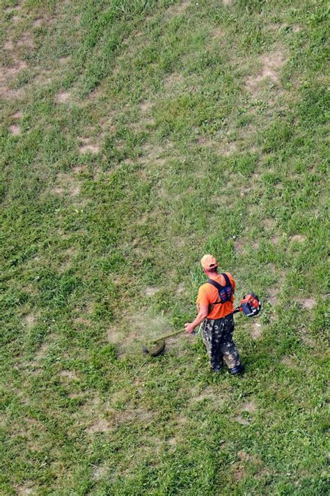 A Worker With A Lawn Mower Mows The Grass Top View A Man In An Ora