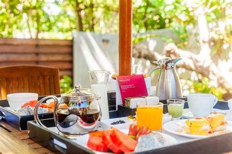 아침 식사는 고급 리조트 또는 호텔의 빌라에있는 개인 열대 정원에서 제공됩니다 계란 베네딕트 신선한 패스트리 과일 주스 및 커피 컵이 테이블에 담긴 트레이 여름 여행 휴일