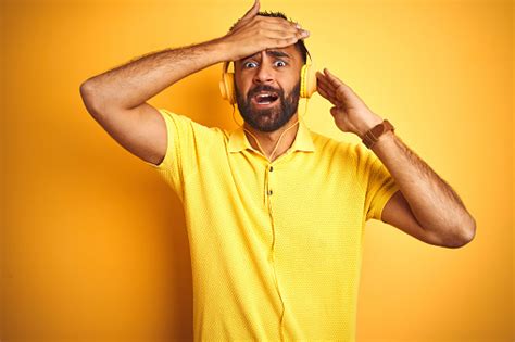 고립 된 노란색 배경 위에 헤드폰을 사용하여 음악을 듣고 아랍 인도 히스패닉 남자는 머리에 손으로 스트레스 수치와 깜짝 얼굴 분노와 좌절에 충격 실수에 대한 두려움과 화가